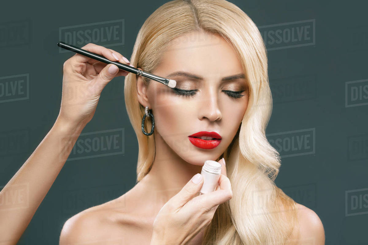 Gorgeous blonde woman applying makeup, isolated on grey - Stock Photo ...