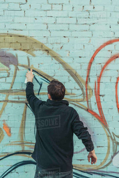 Back view of man painting colorful graffiti on wall - Royalty-free ...