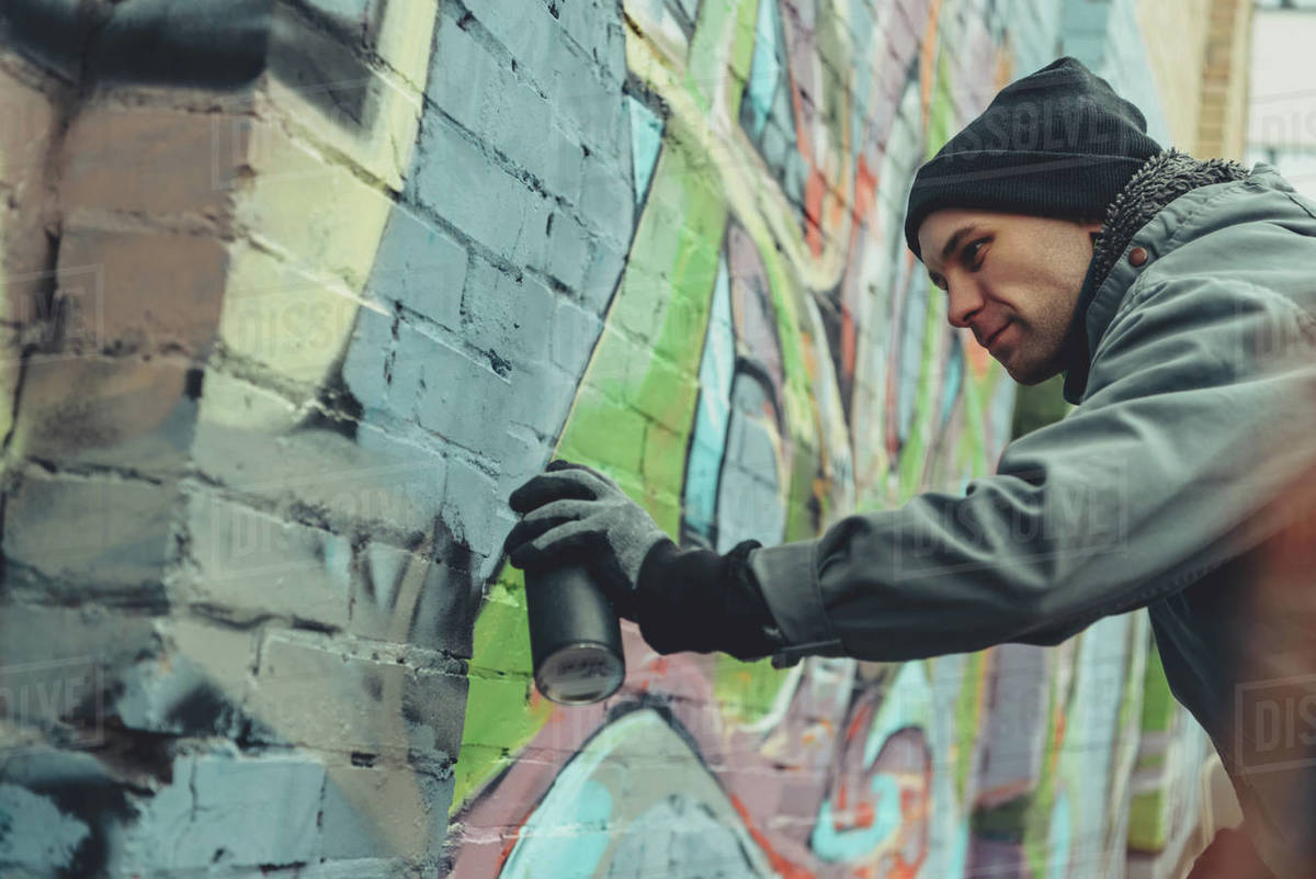 Male street artist painting colorful graffiti on wall - Stock Photo ...