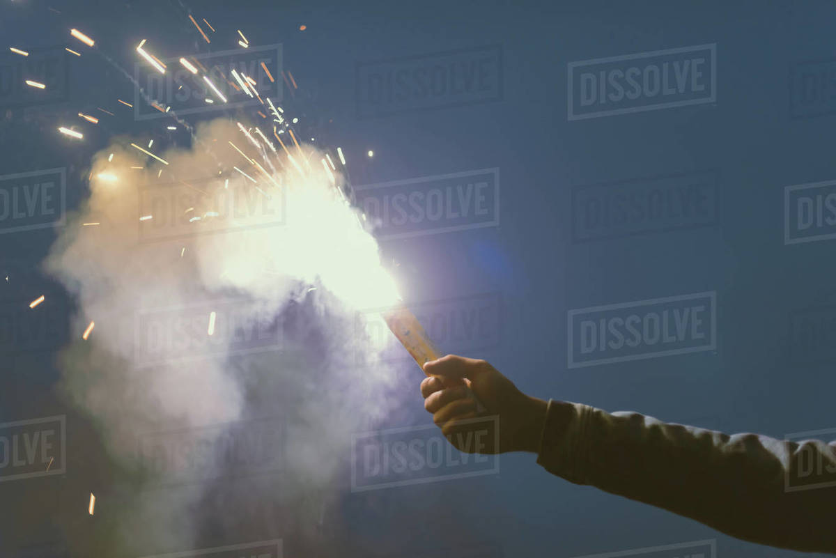 Cropped view of male hand with smoke bomb with sparks at night ...