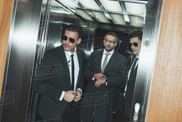 Bodyguards looking out from elevator and businessman looking at watch ...