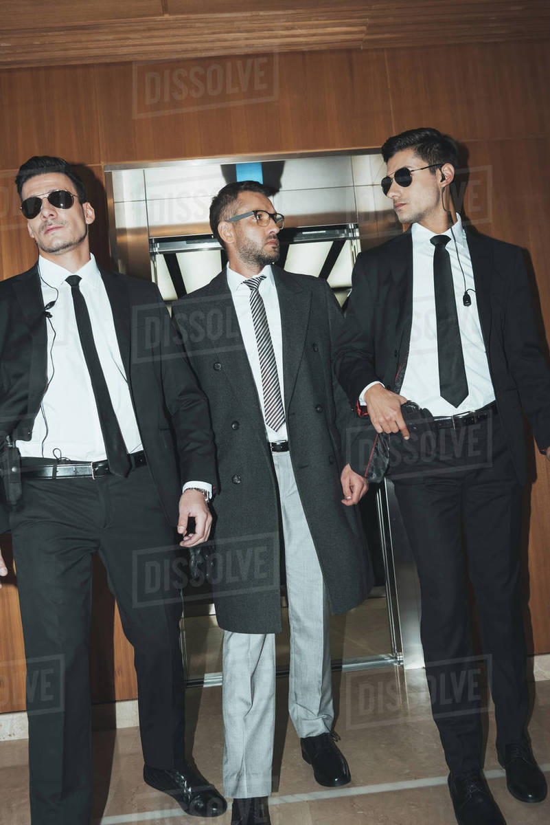 Bodyguards and businessman walking from elevator in business center ...