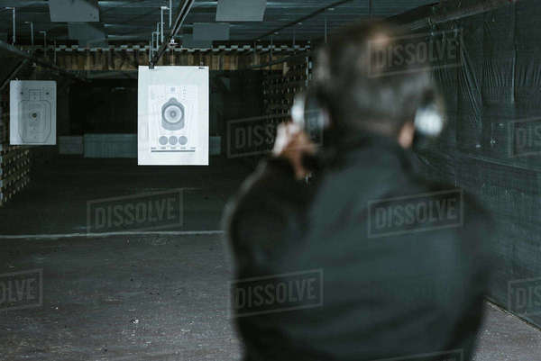 Rear view of man aiming gun at target in shooting range - Royalty-free ...