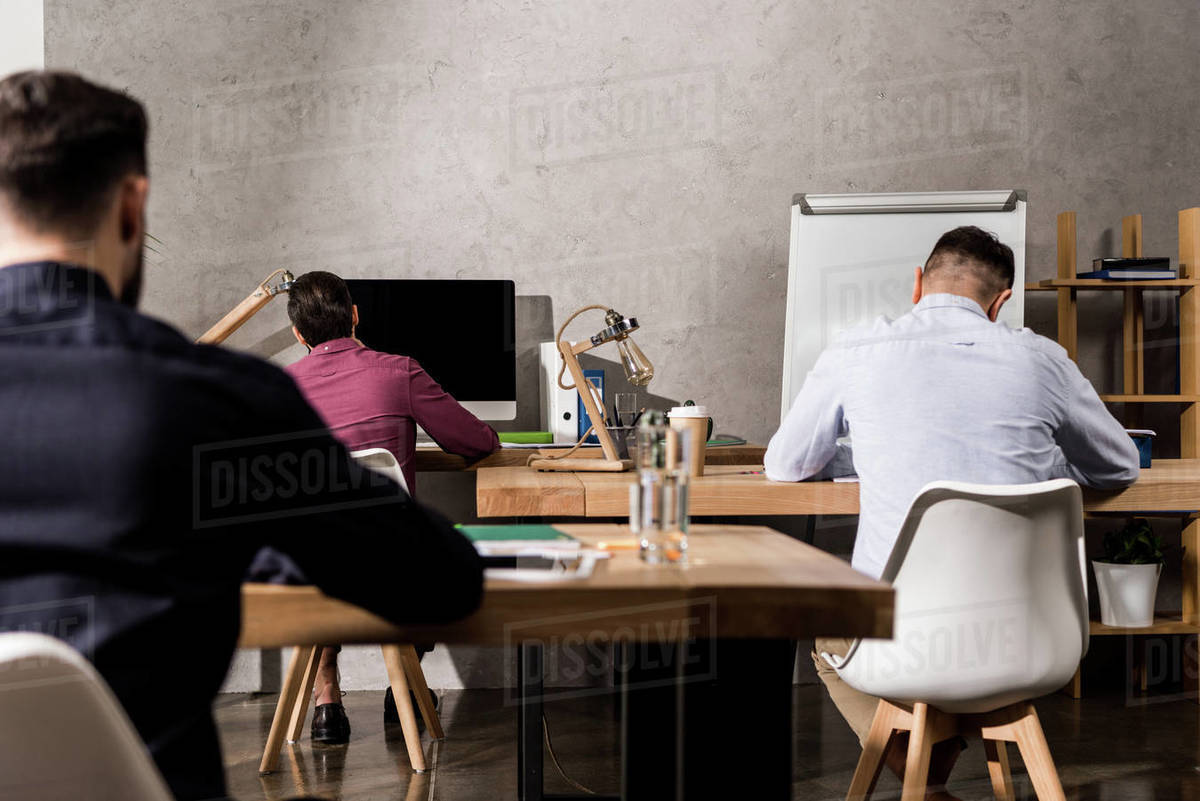 Rear view of businessmen sitting at working tables in office - Royalty ...