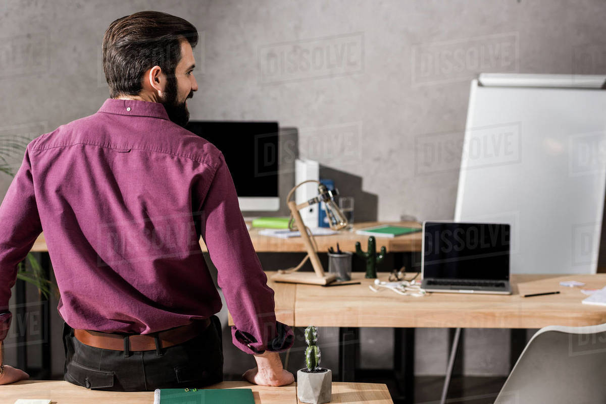 Rear view of businessman leaning on table in office - Royalty-free ...