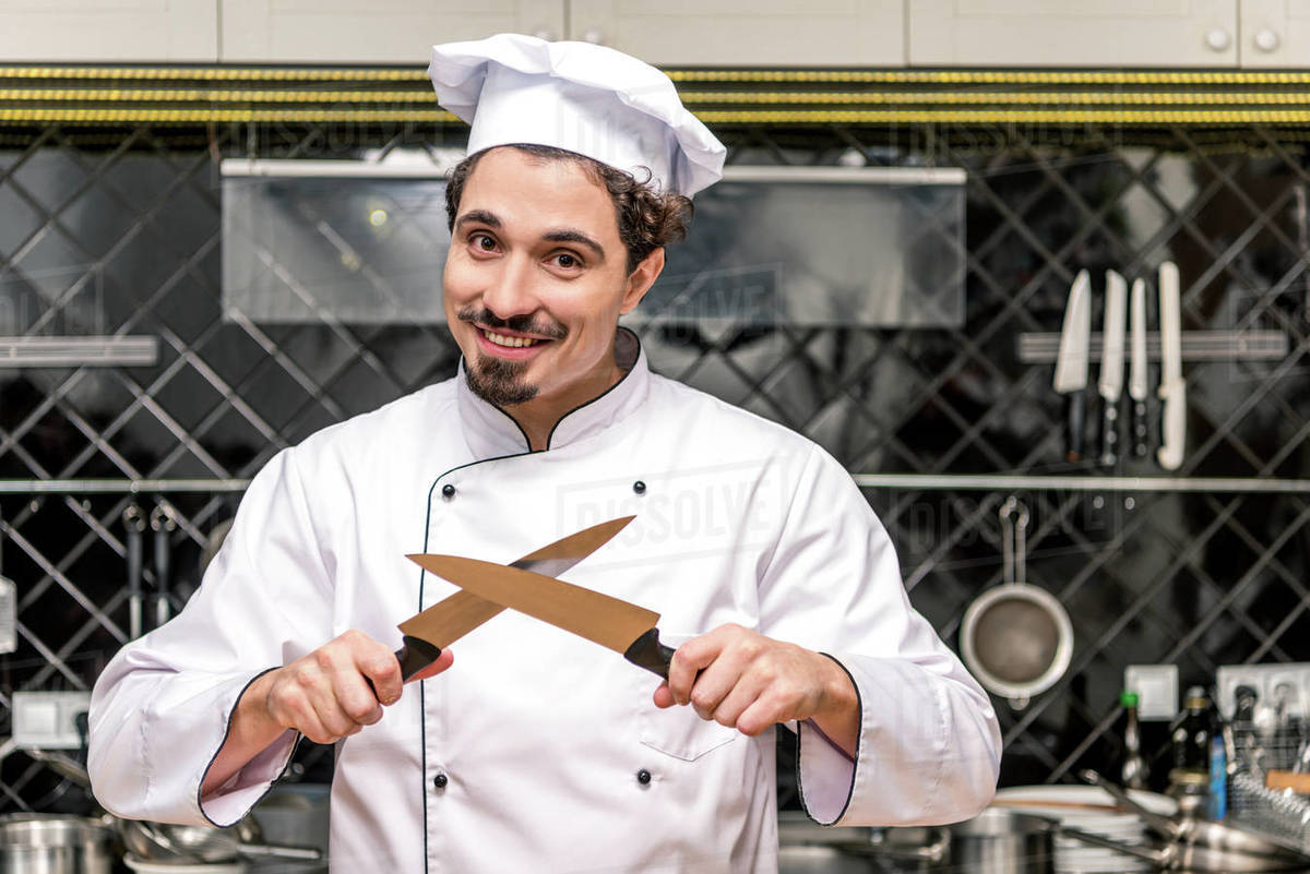 smiling chef standing with crossed knifes - Stock Photo - Dissolve