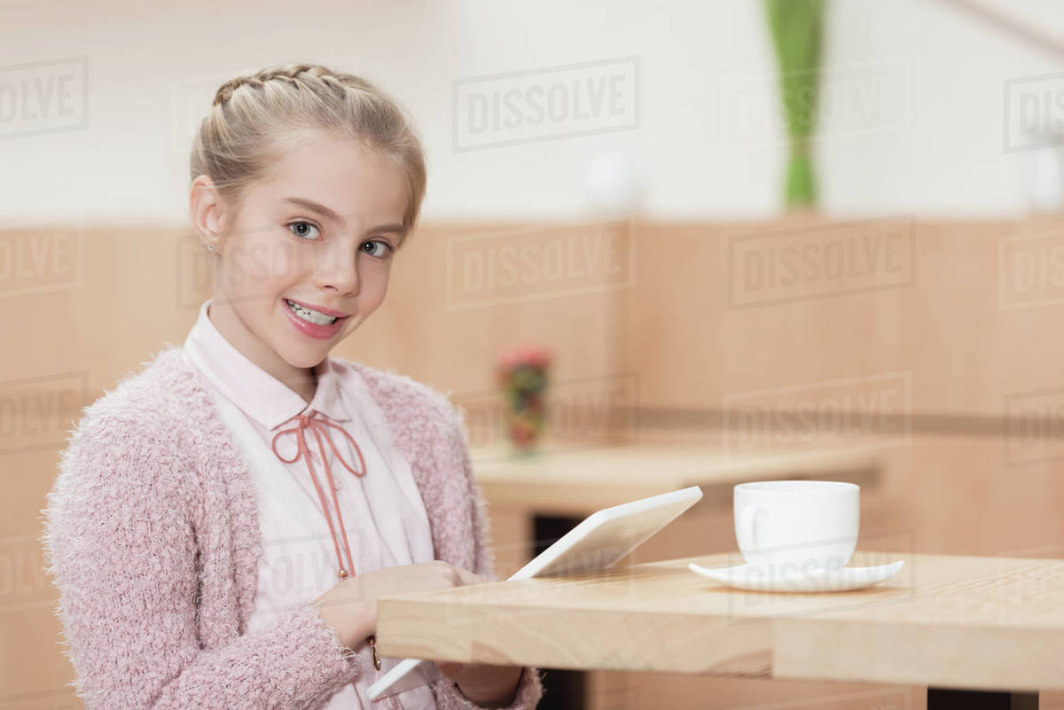 smiling child with digital tablet looking at camera while sitting at ...