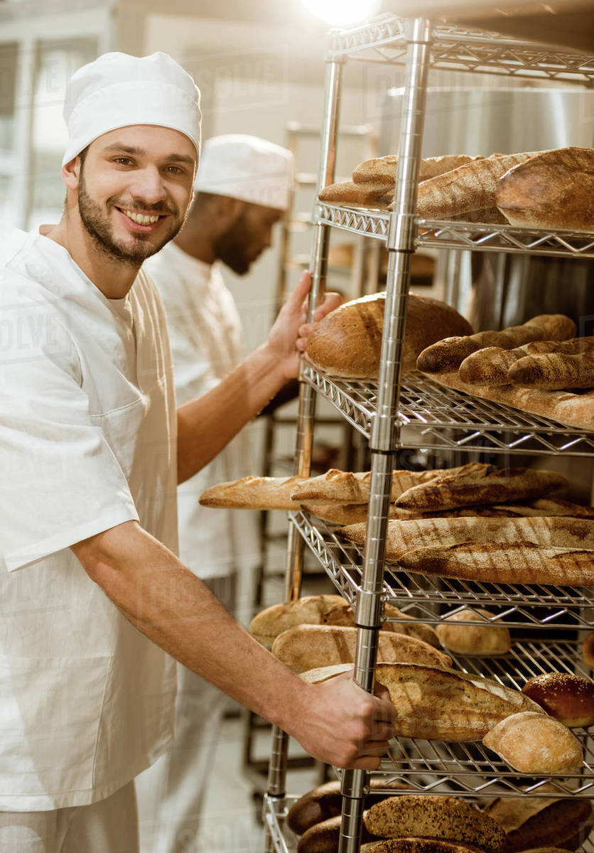Baker near shelves with fresh bread loaves at baking manufacture ...