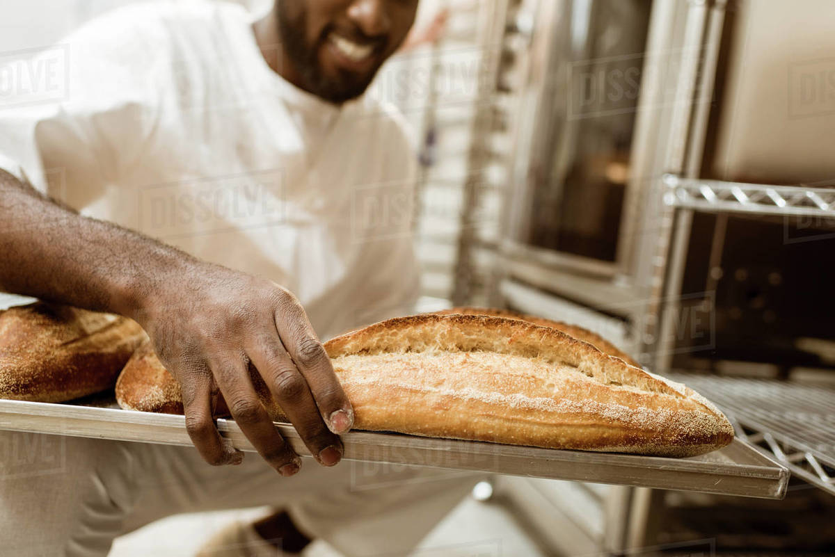 Cropped shot of african american baker with tray of fresh loaves of ...