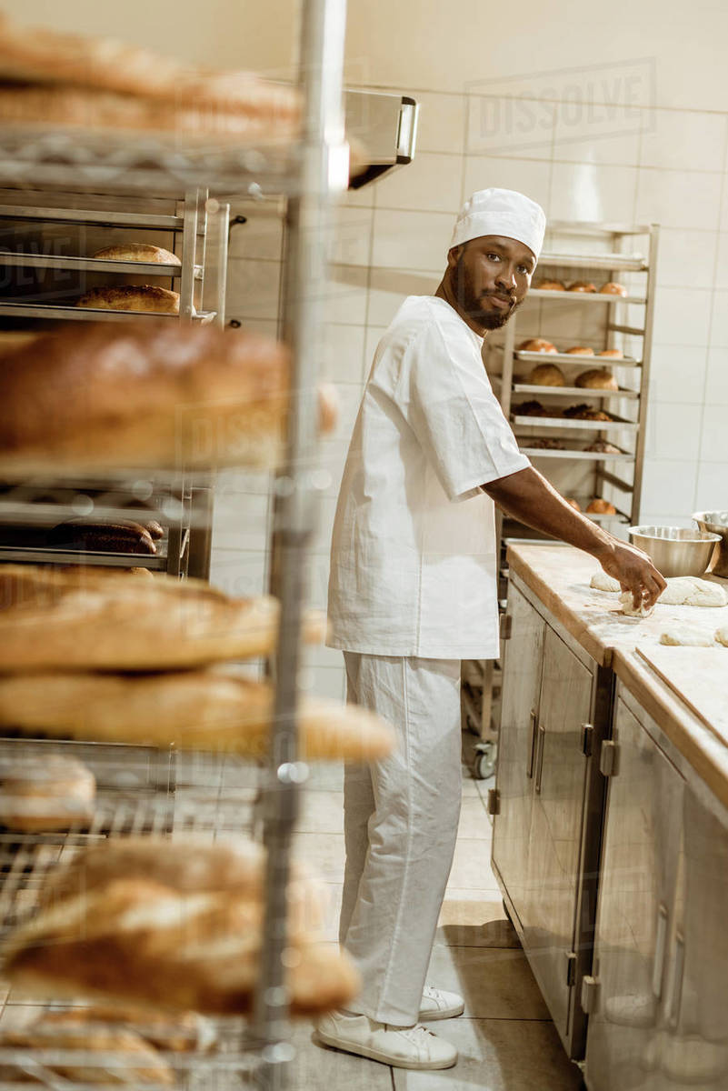 African american baker preparing raw dough at workplace on baking ...