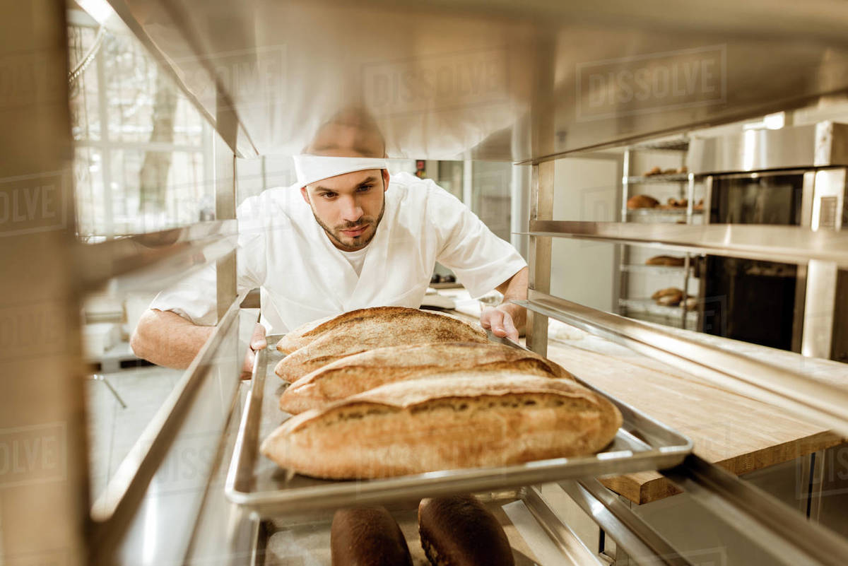 Professional baker putting trays of fresh bread on stand at baking ...
