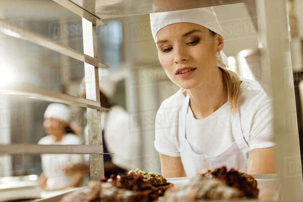 Beautiful female baker looking at tray of freshly baked croissants on ...