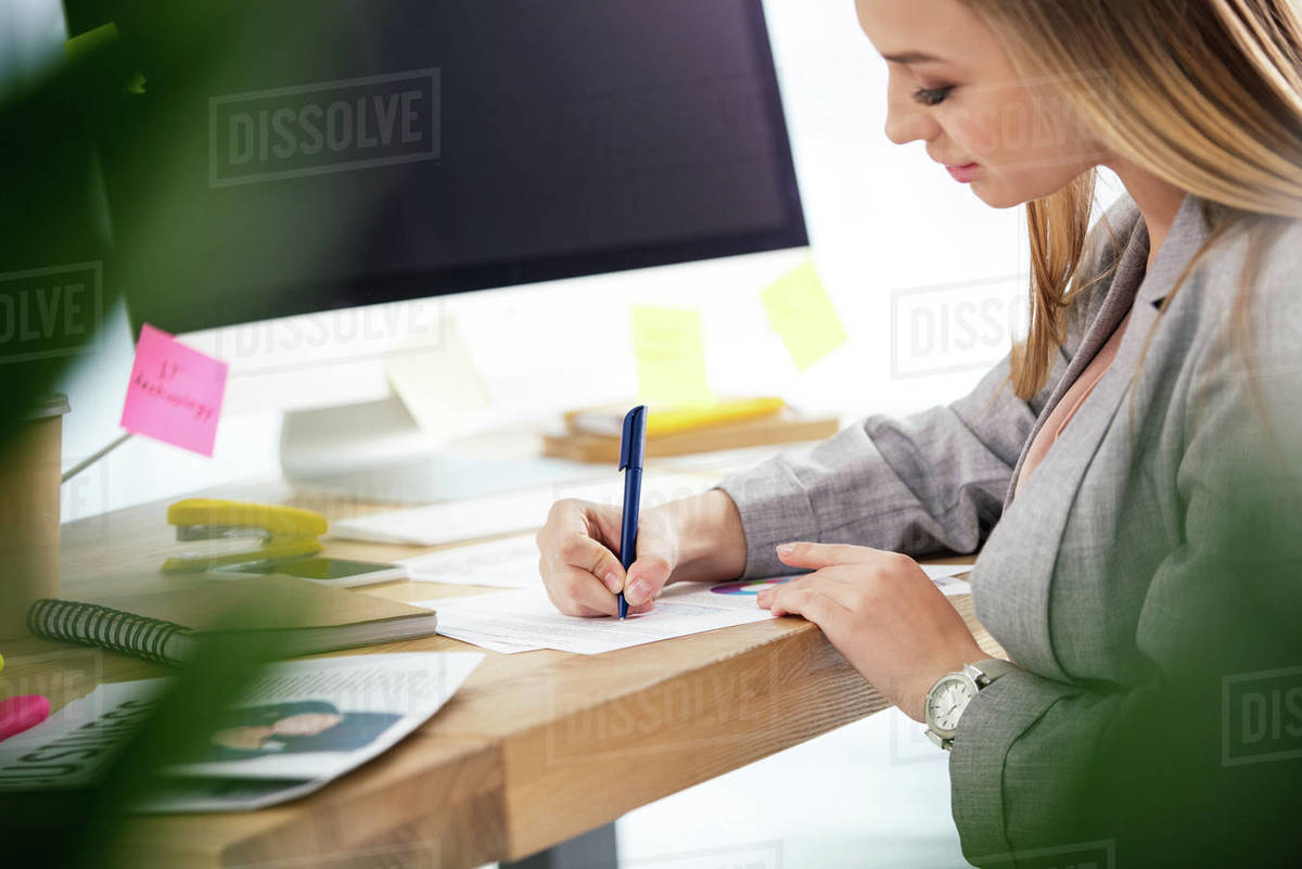 Side view of female marketing manager doing paperwork at workplace in ...