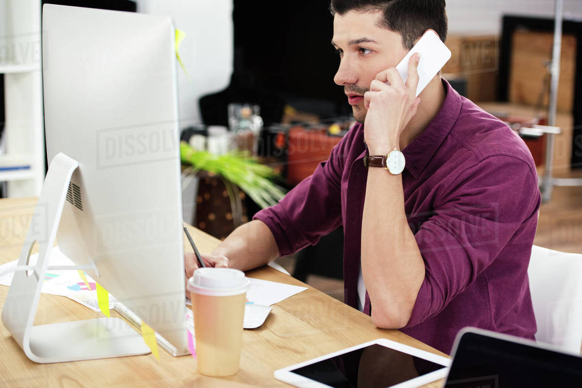 Side view of focused businessman talking on smartphone at workplace in ...