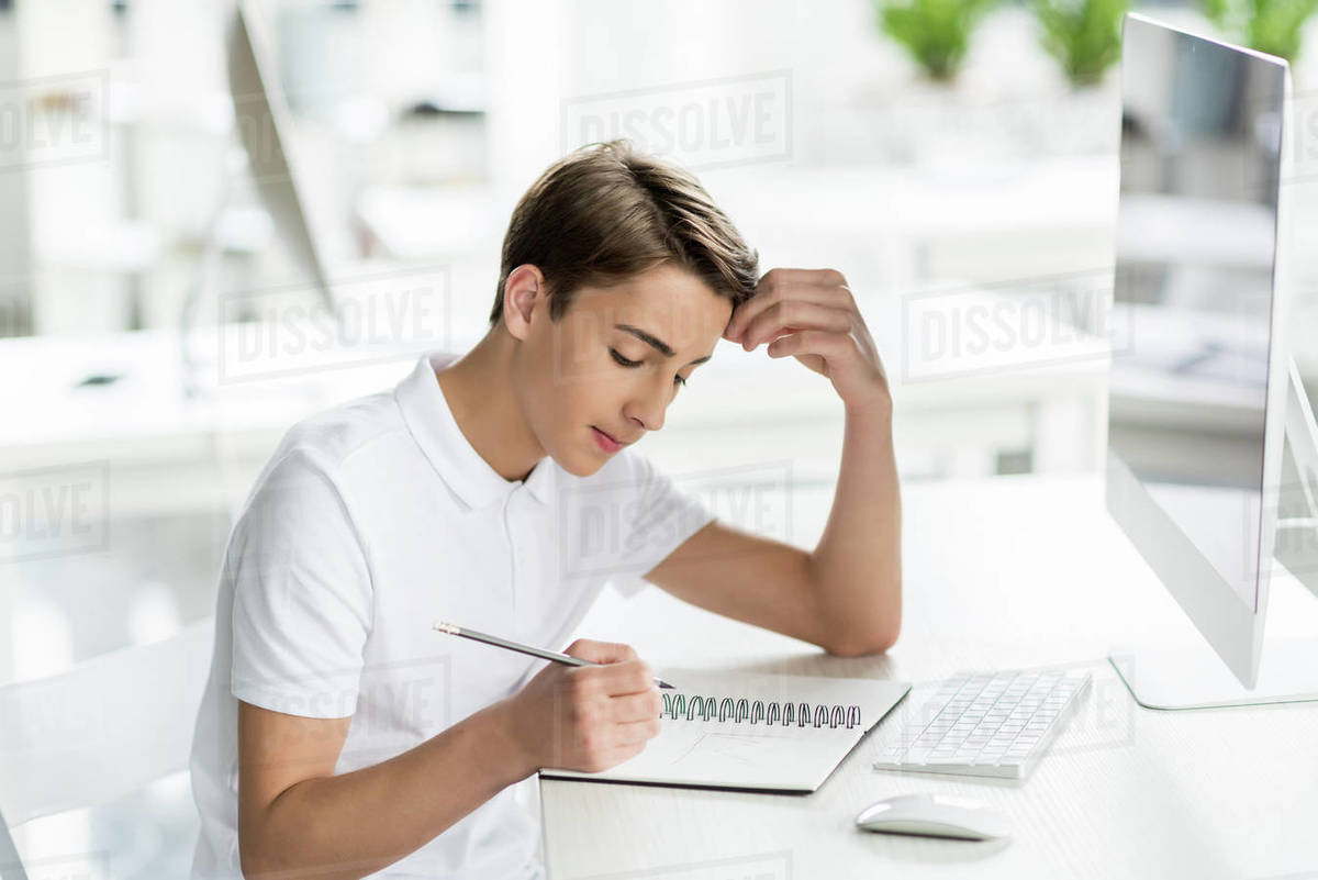 Side view of focused student doing task while sitting at table with ...
