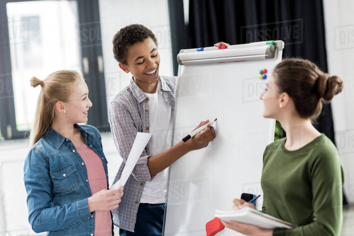 African American boy writing on white board while discussing project ...