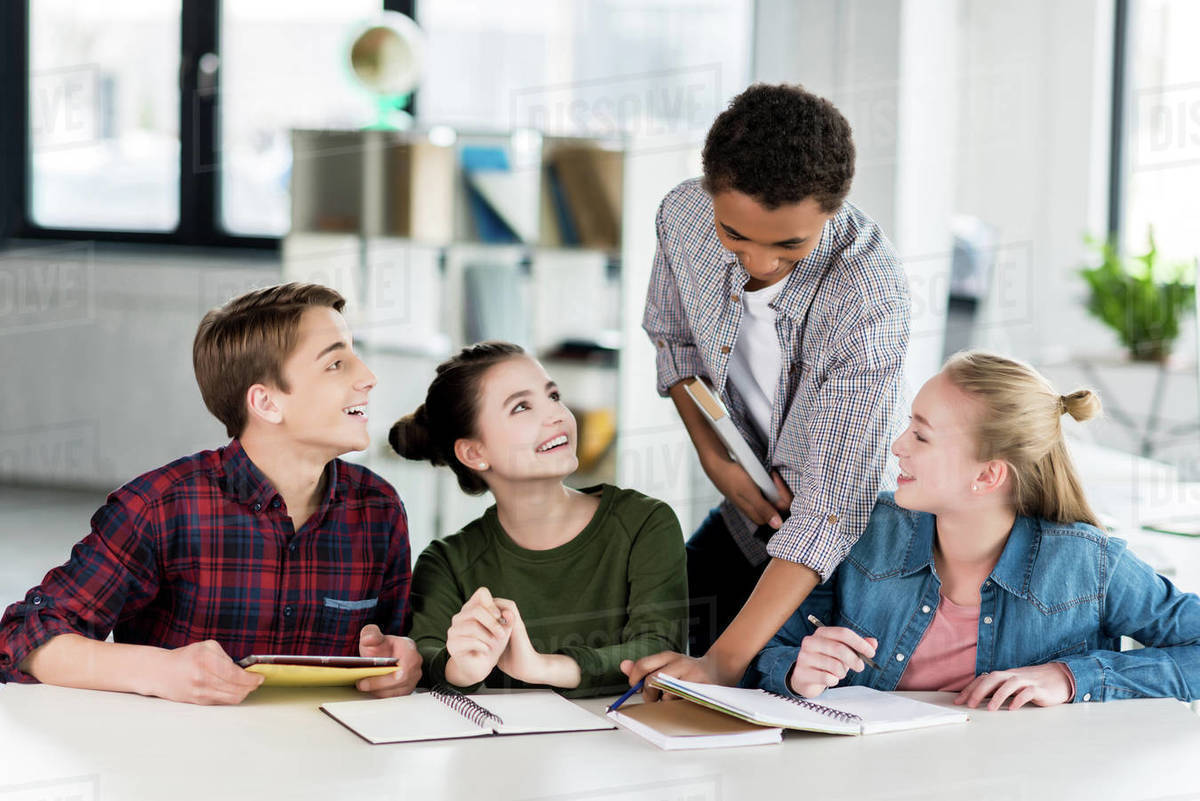 Multiethnic group of teenagers doing homework together in class ...