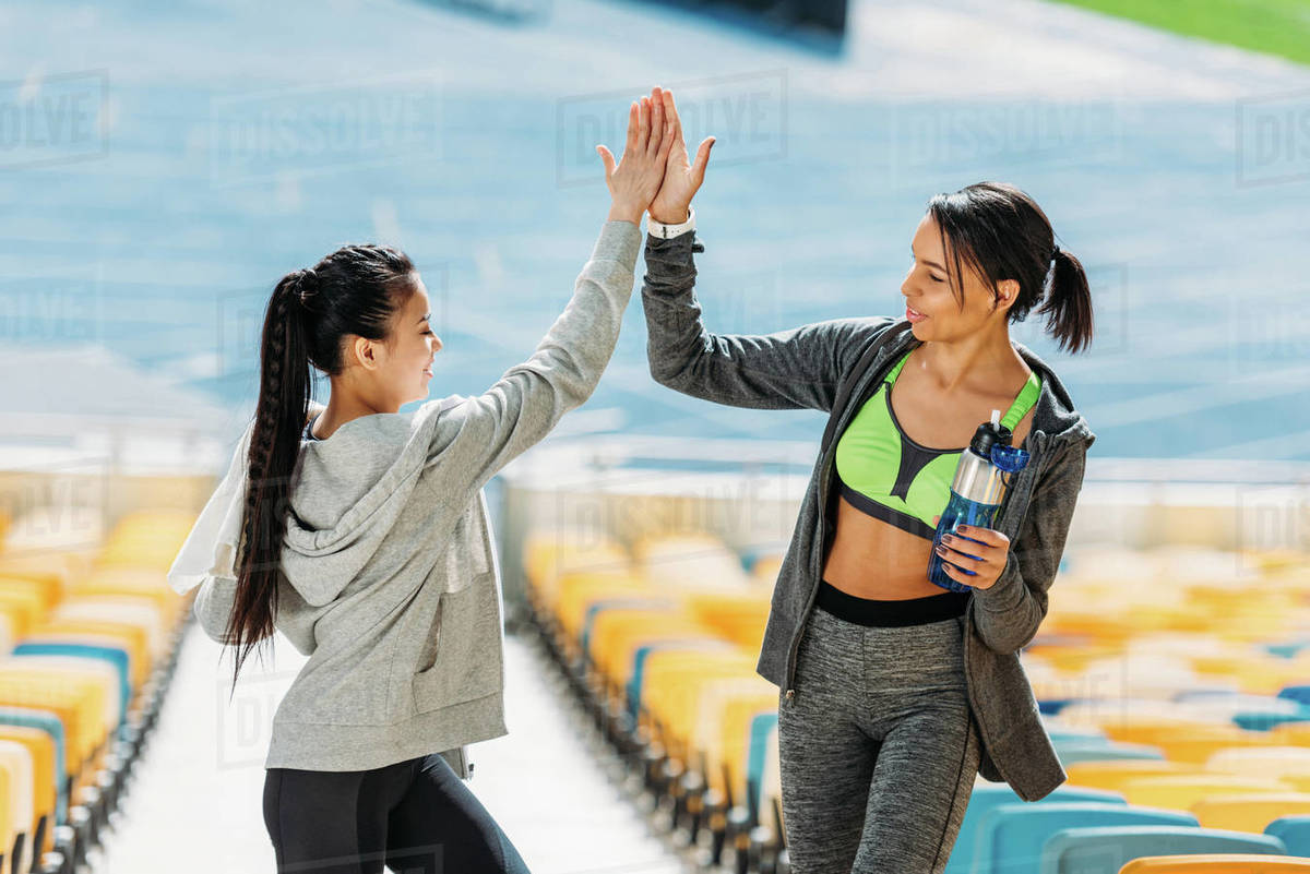 Two young sportswomen with sport bottle giving high-five on stadium ...