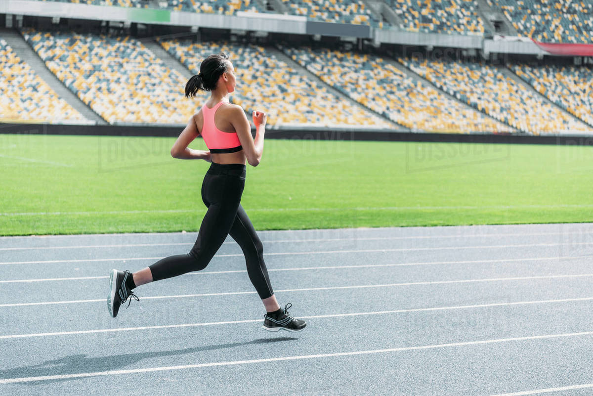 Side view of athletic young woman in sportswear sprinting on running ...