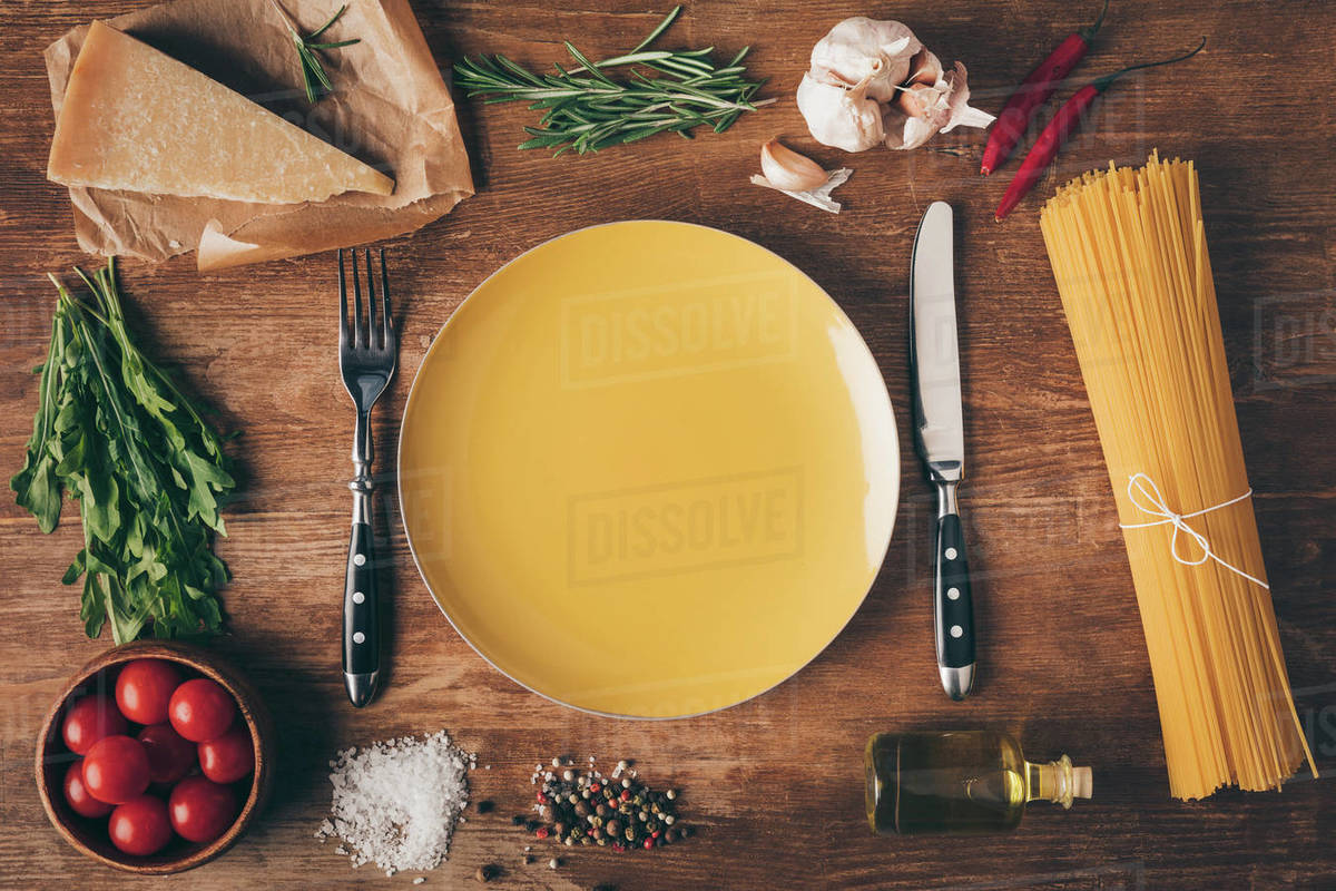 Top view of row pasta, fresh ingredients and plate with knife and fork ...