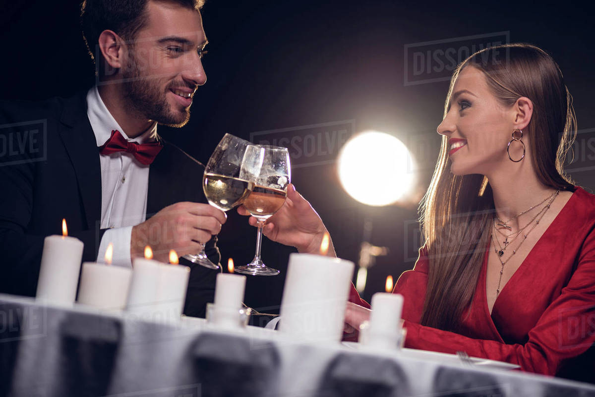 Couple clinking with wine glasses on romantic date in restaurant ...
