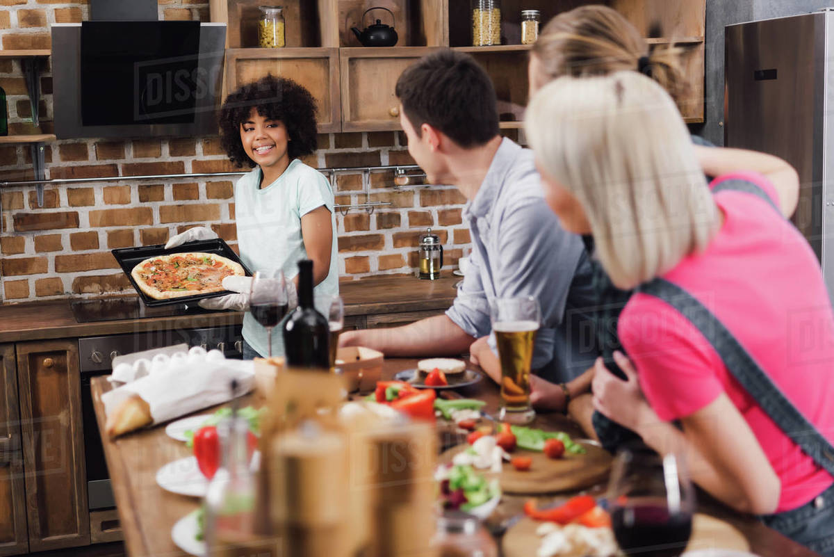 Smiling African American girl bringing homemade pizza to friends ...