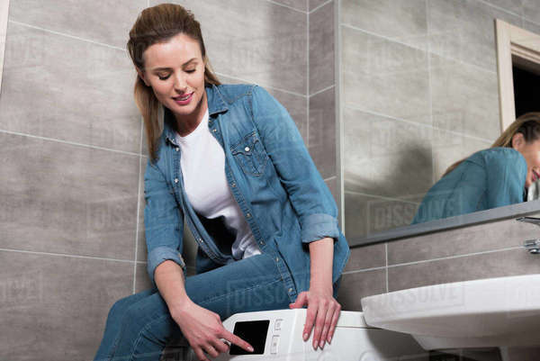 Portrait of attractive housewife operating washing machine at home ...