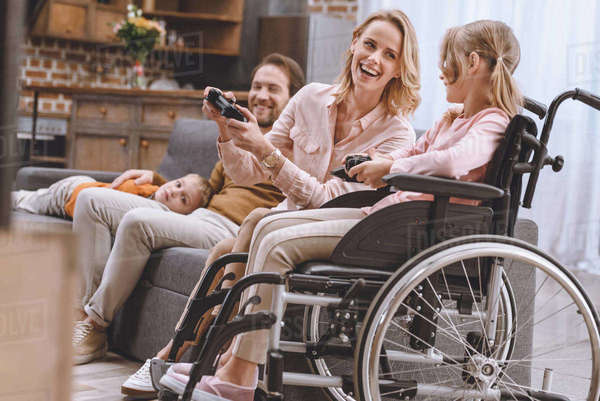 family with disabled child in wheelchair playing with joysticks ...