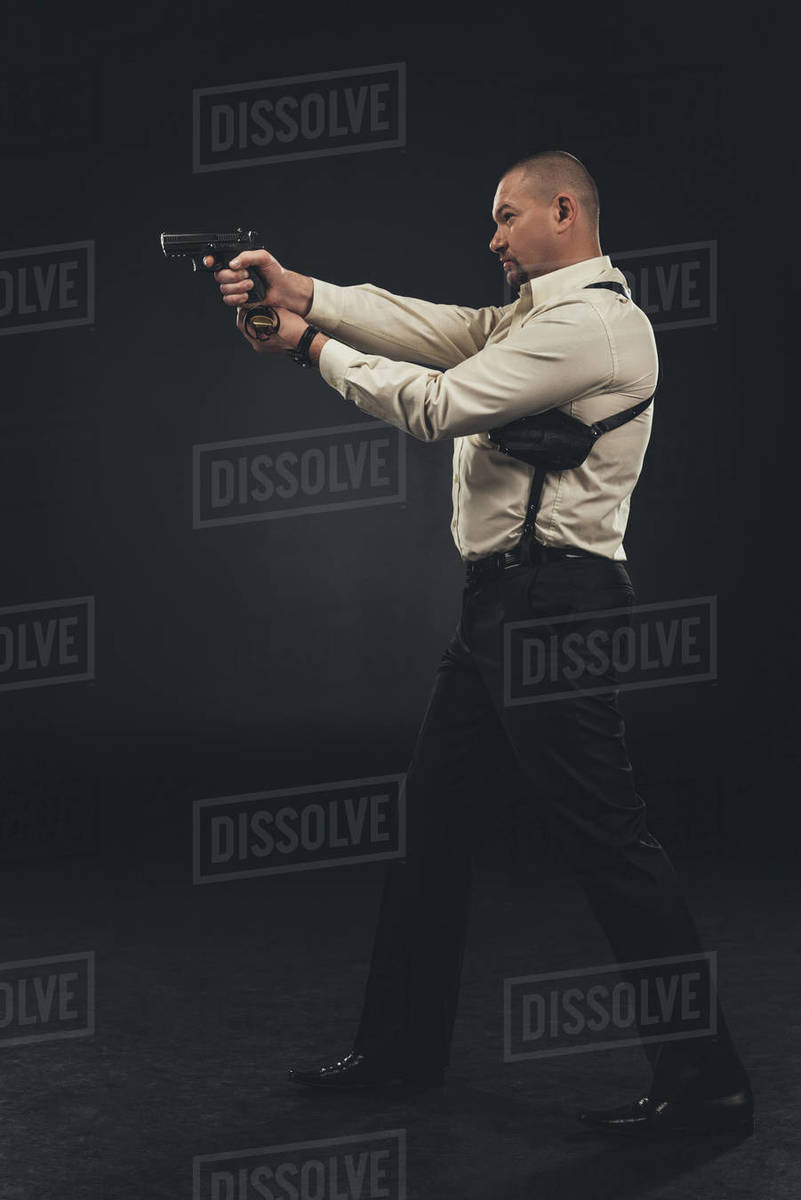 Side view of security man holding gun on black - Stock Photo - Dissolve