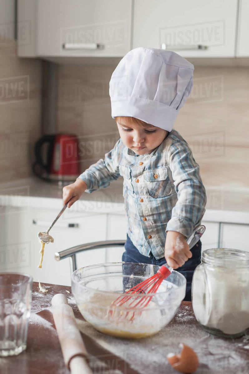 adorable little kid in chef hat mixturing dough with whisk at kitchen ...