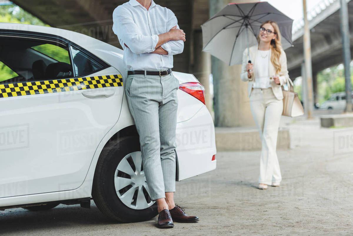 Cropped shot of man leaning at cab while smiling girl with umbrella ...