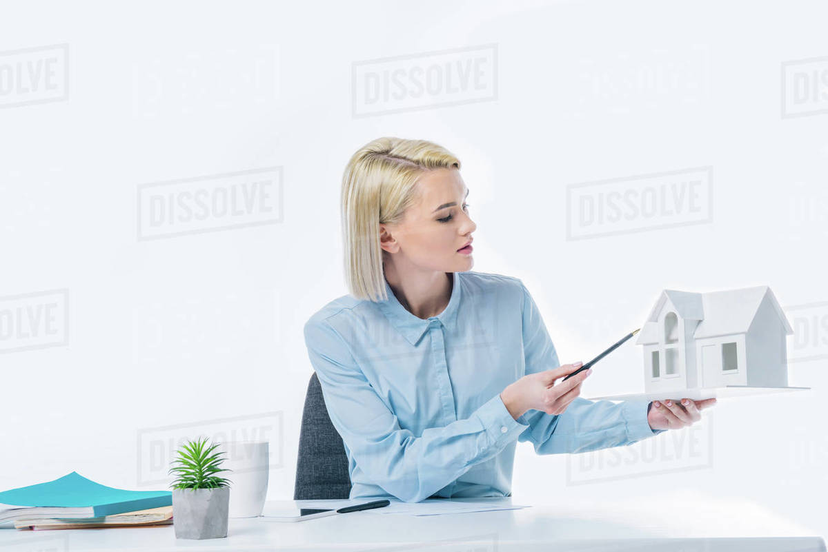 Portrait of real estate agent pointing at house model in hand at ...