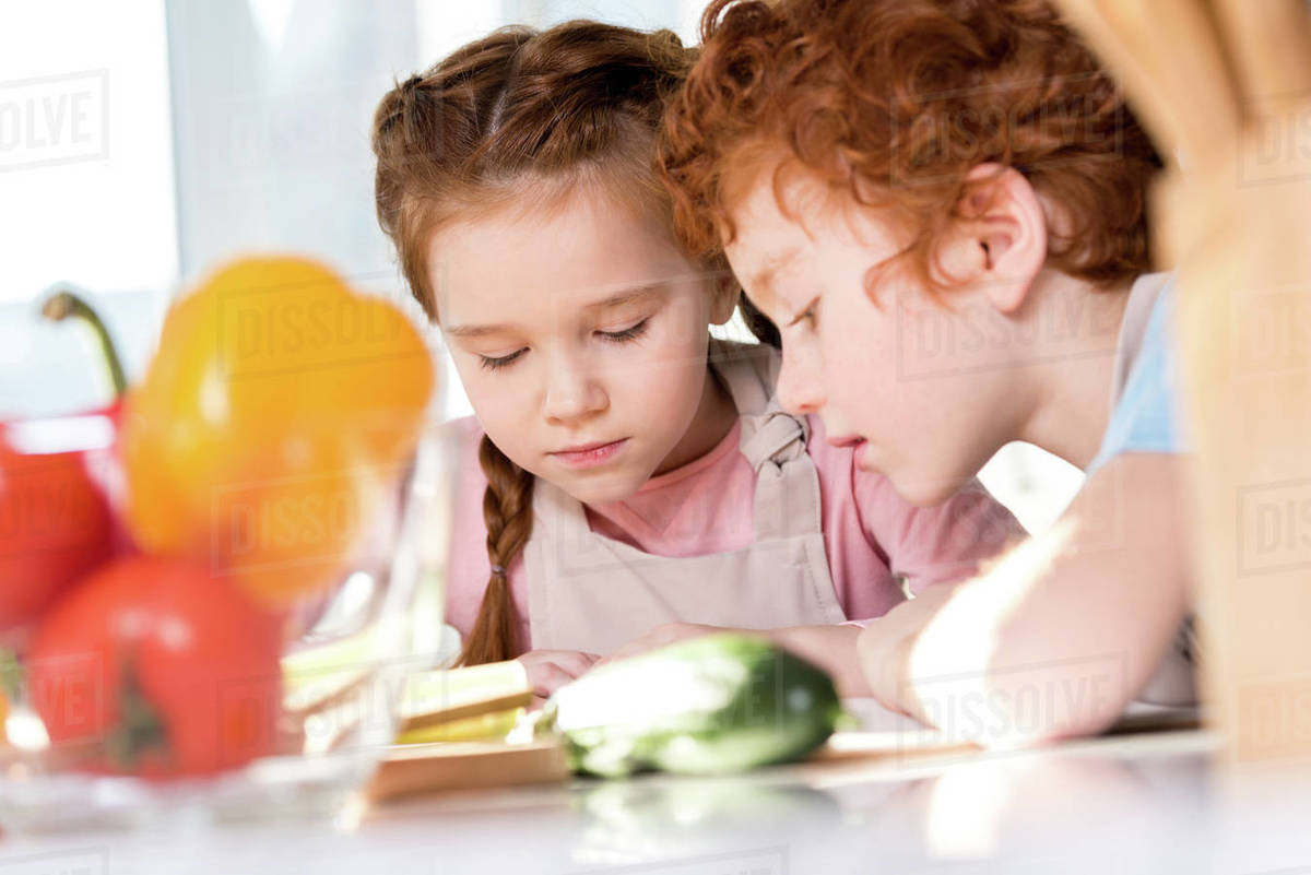 Focused children reading cookbook while cooking together in kitchen ...