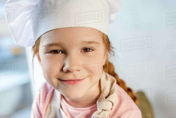 Adorable little kid in chef hat smiling at camera - Stock Photo - Dissolve