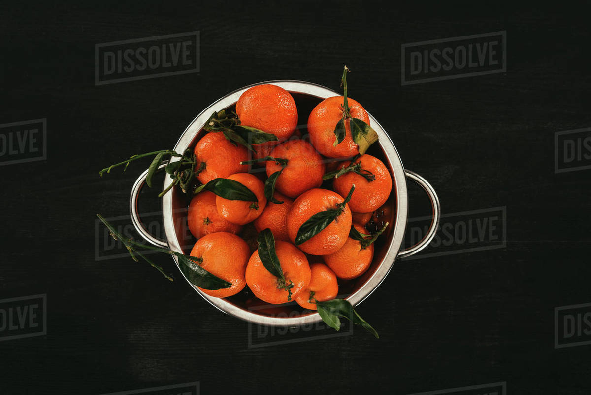 top view of pile of mandarins in saucepan on black wooden surface ...