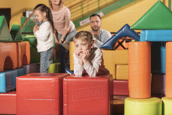 bored little boy looking away while family playing with colorful blocks ...