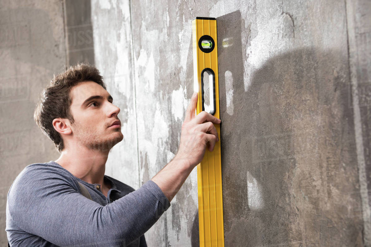 Professional young worker measuring wall with level tool, renovation ...