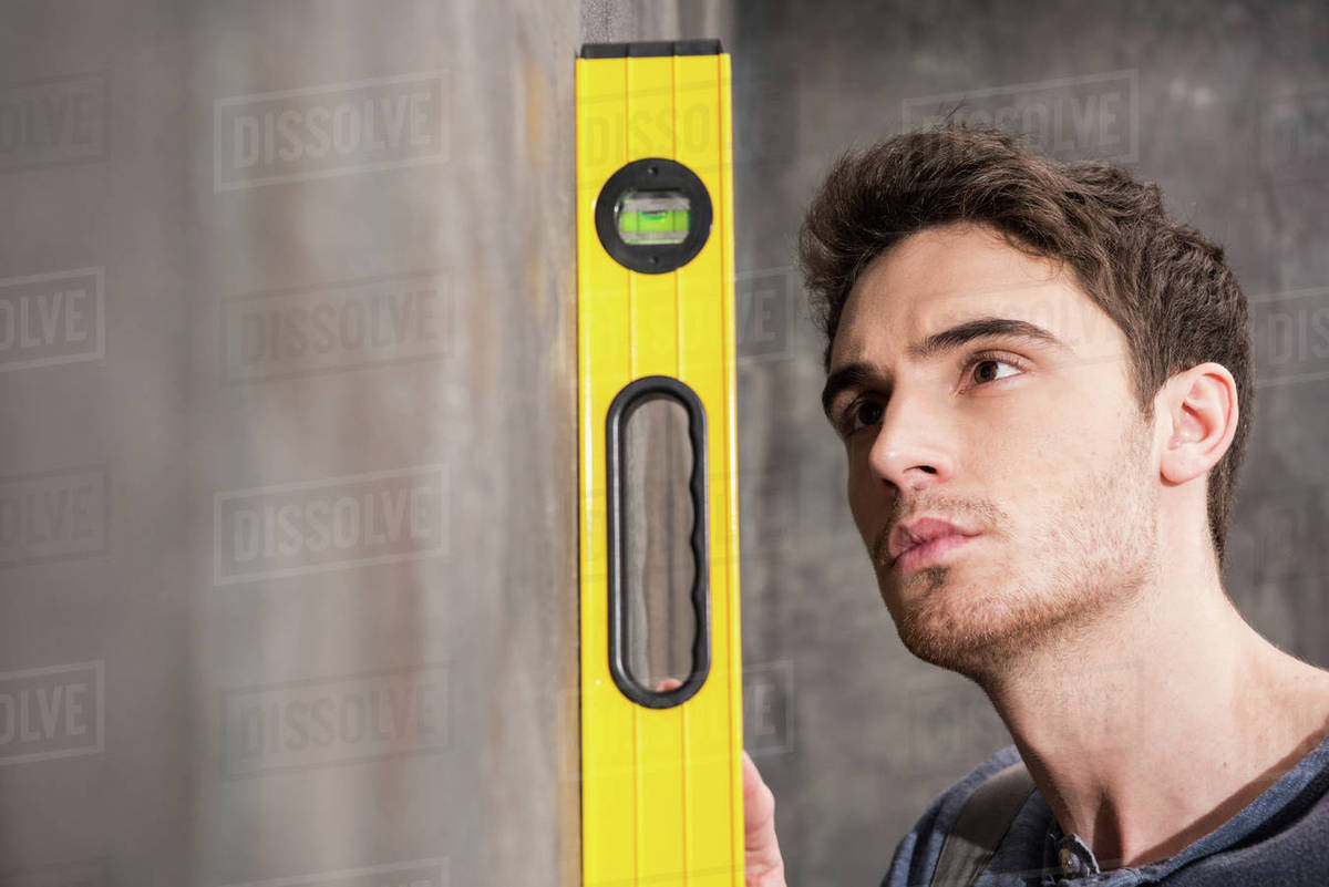 Professional young worker measuring wall with level tool, renovation ...