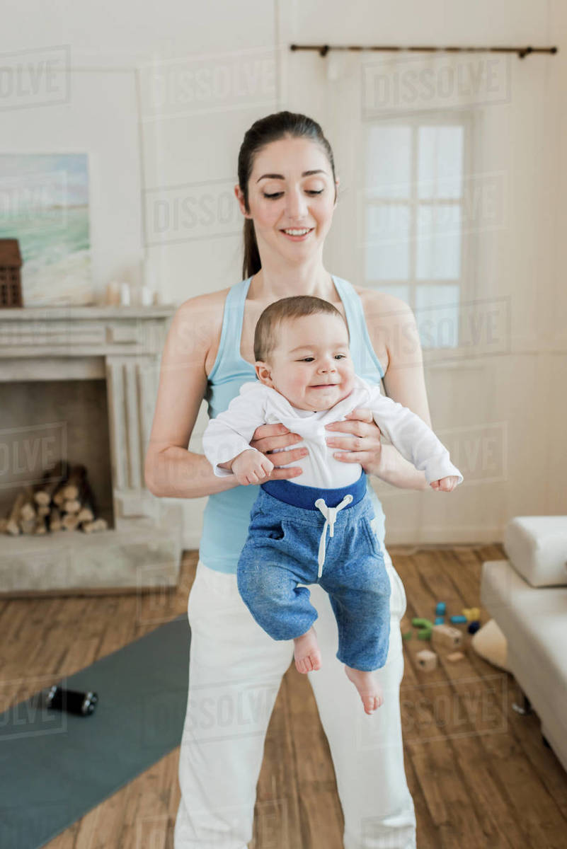Portrait of smiling woman carrying her happy baby child on arms and ...