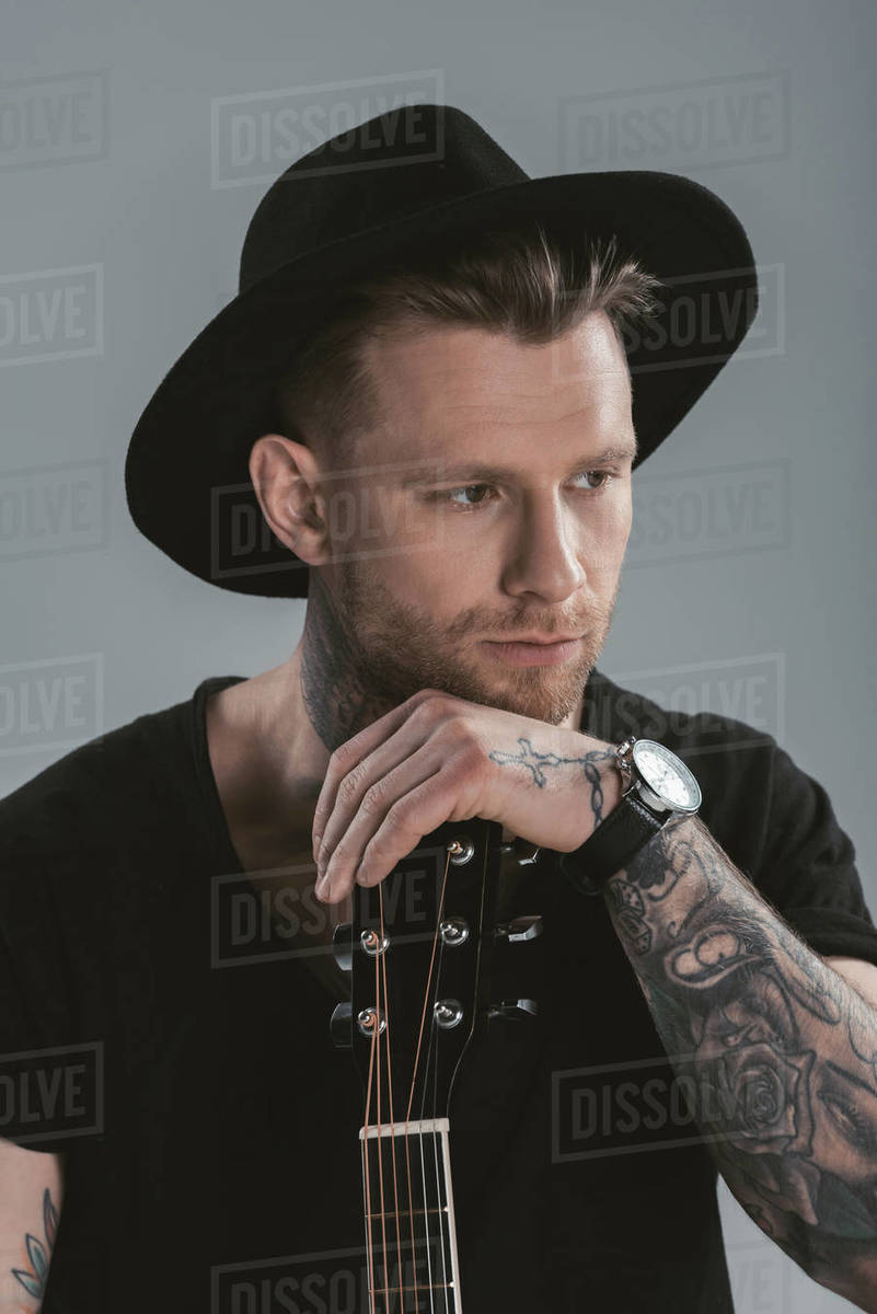 Fashionable guitarist in black hat with guitar, isolated on grey ...
