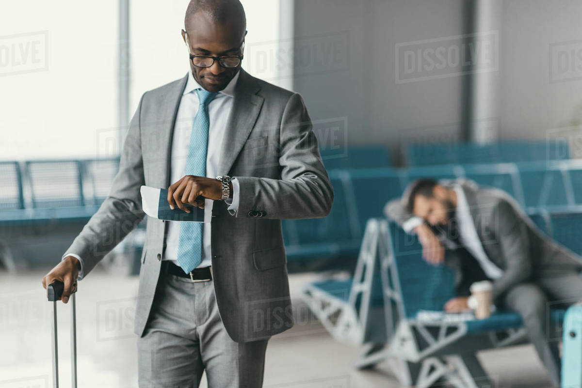 Handsome businessman looking at watch while waiting for flight in ...