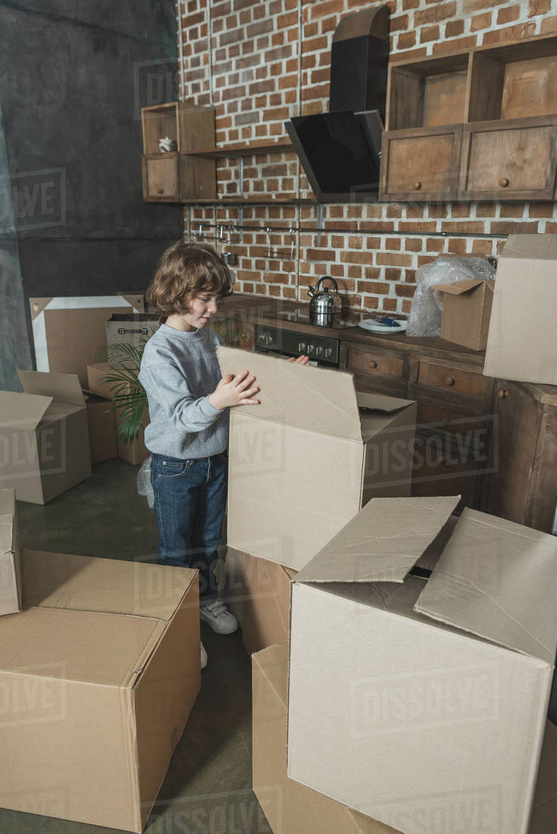 Adorable little boy unpacking cardboard boxes in new apartment ...