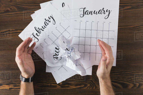 Cropped shot of male hands and teared calendar on wooden tabletop ...