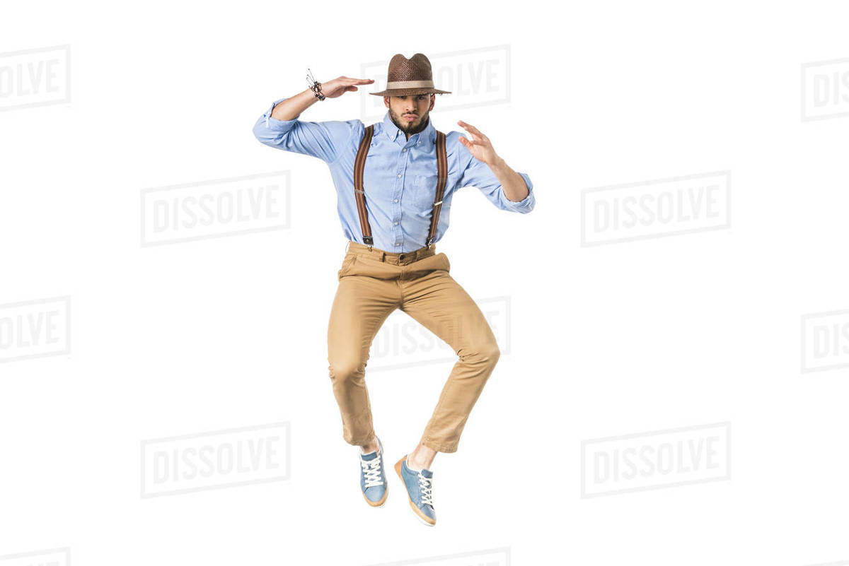 Stylish young man in hat jumping and looking at camera isolated on ...
