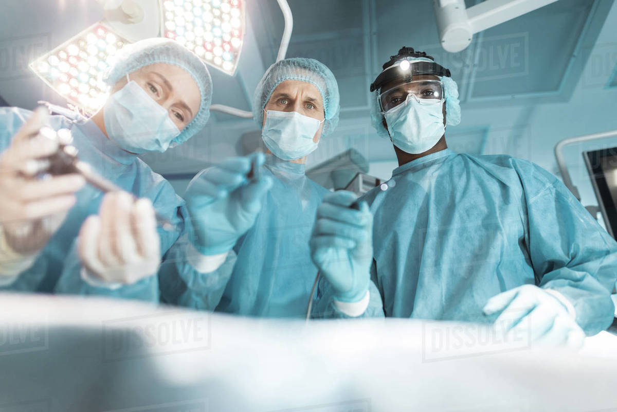 Bottom view of multicultural surgeons looking at patient during surgery ...