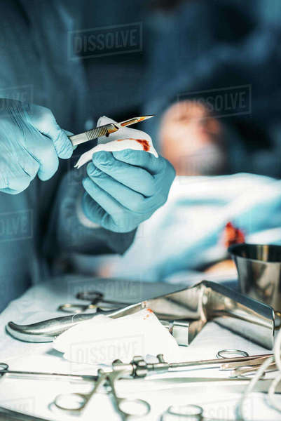 Cropped image of surgeon cleaning scalpel from blood in surgery room ...