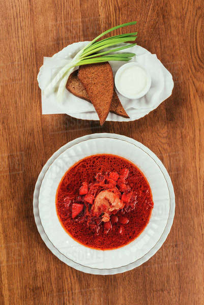 Top view of borscht dish in white plate served with rye bread on wooden ...