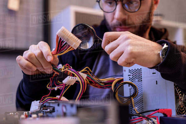Man holding wires in hand and using magnifier while fixing pc - Royalty ...