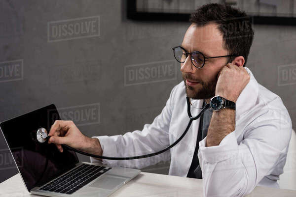 Repairman in doctor white coat using stethoscope to diagnose laptop ...