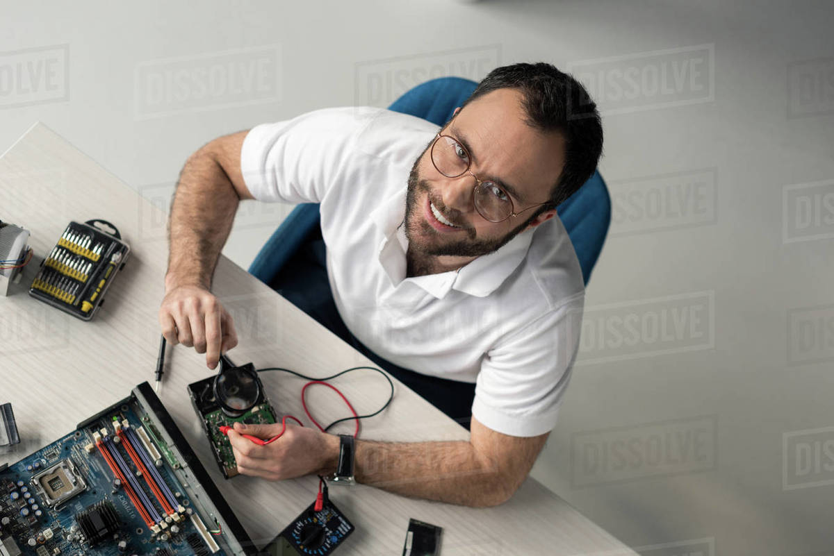 Overhead view of smiling man holding multimeter and magnifier in hands ...